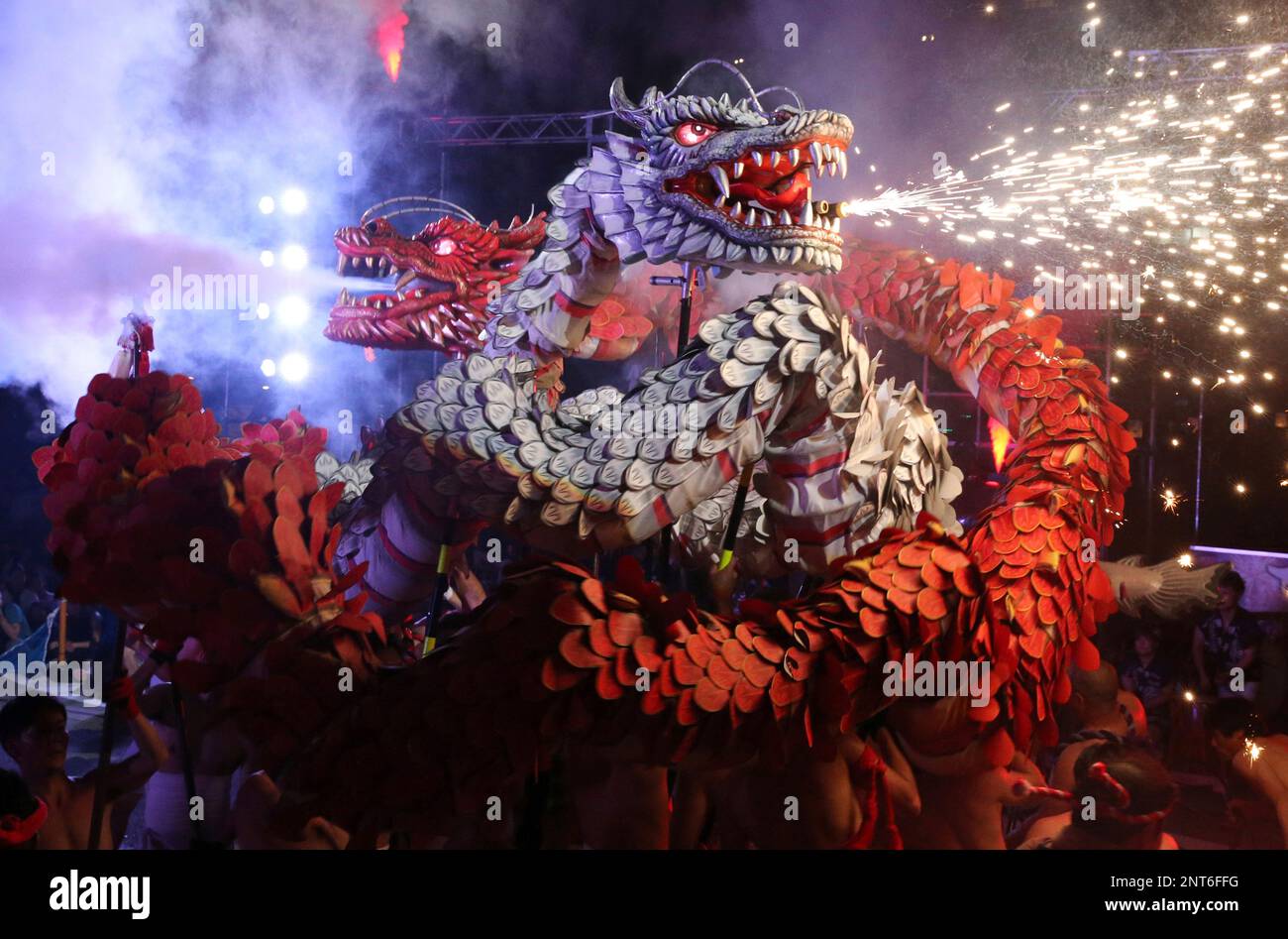 People clad in a loincloth carry a dragon float, portable shrine, and ...