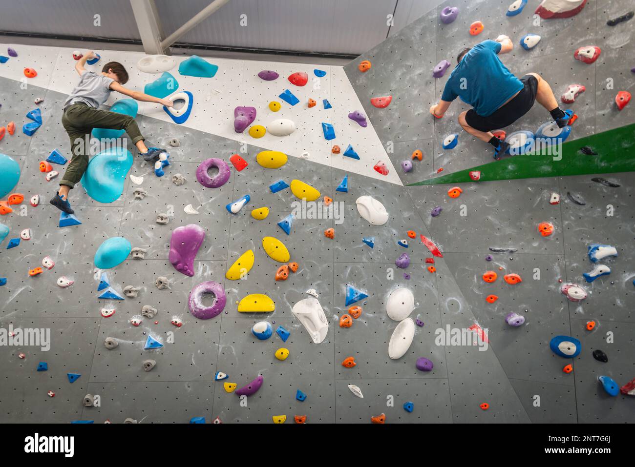 Two people traversing indoor climbing wall using holds and grips of ...