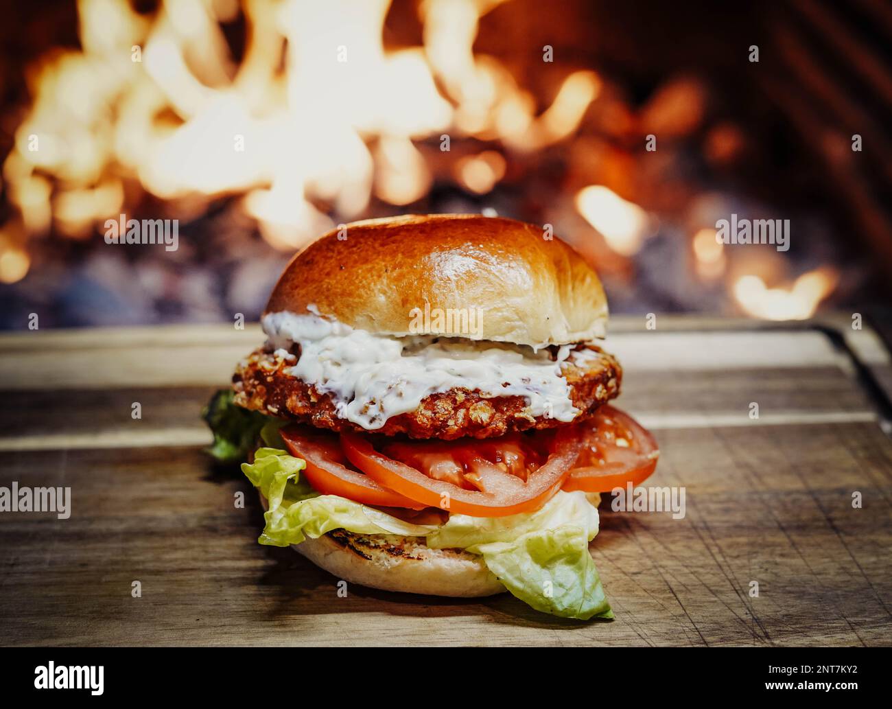 Chicken burger on a wooden table in front of a fireplace Stock Photo ...