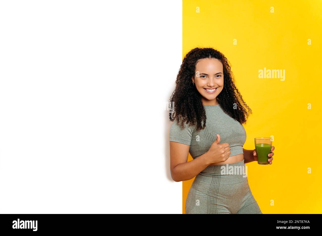 Happy mixed race sporty young woman, in sportswear, holds a glass of ...