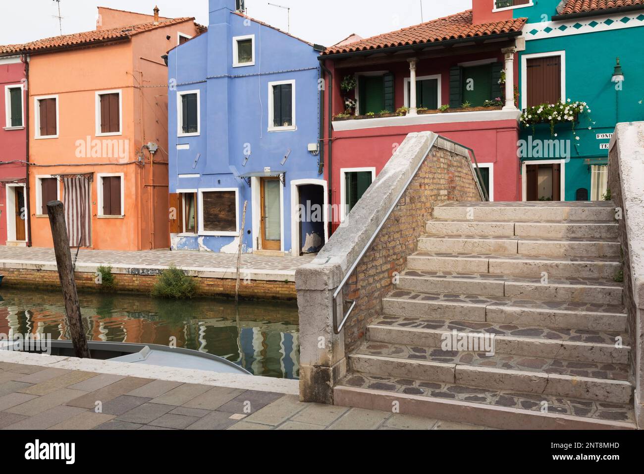 Stone and brick footbridge over canal lined with colourful stucco ...