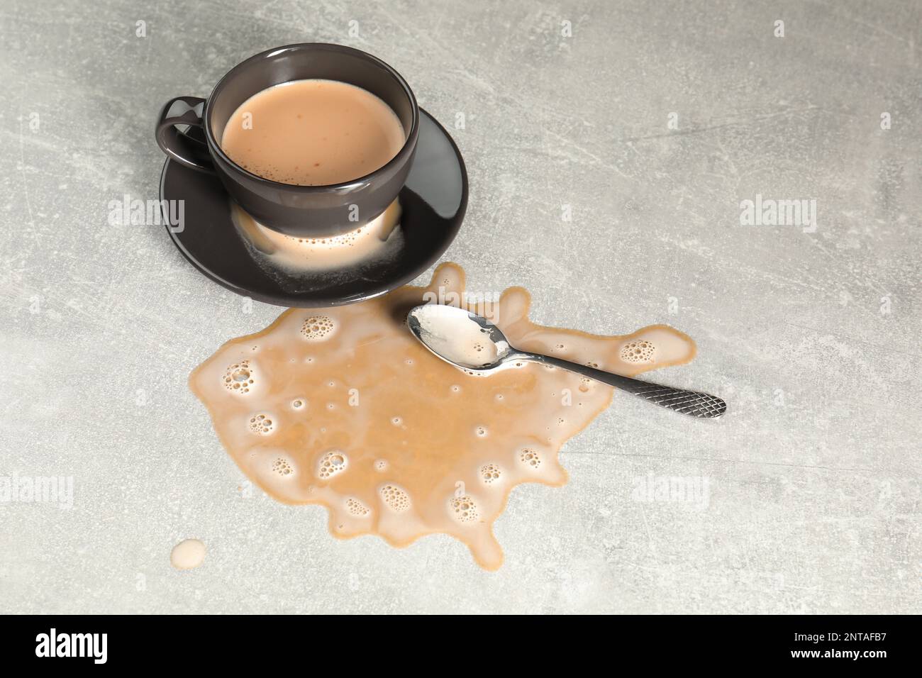 Cup, saucer and spoon near spilled coffee on grey table Stock Photo - Alamy