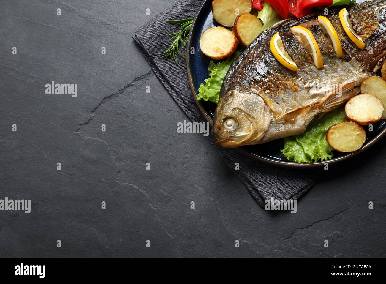 Tasty homemade roasted crucian carp with garnish on black table, top ...