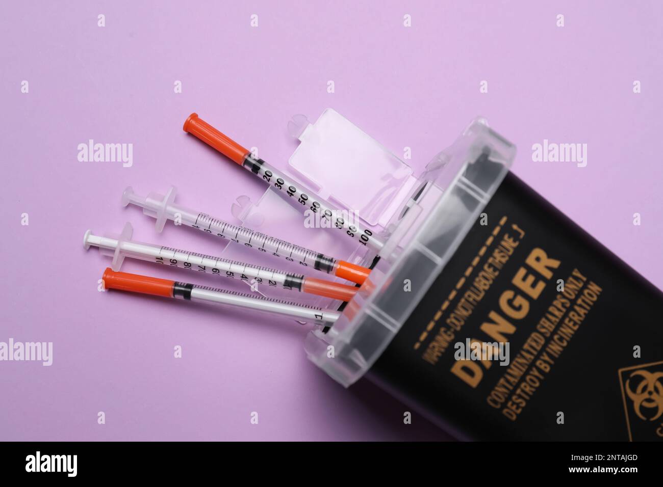 Disposable syringes and sharps container on violet background, top view ...