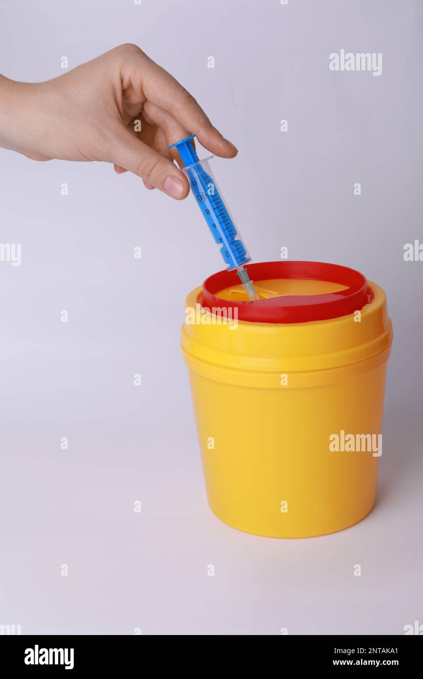 Woman throwing used syringe into sharps container on white background ...