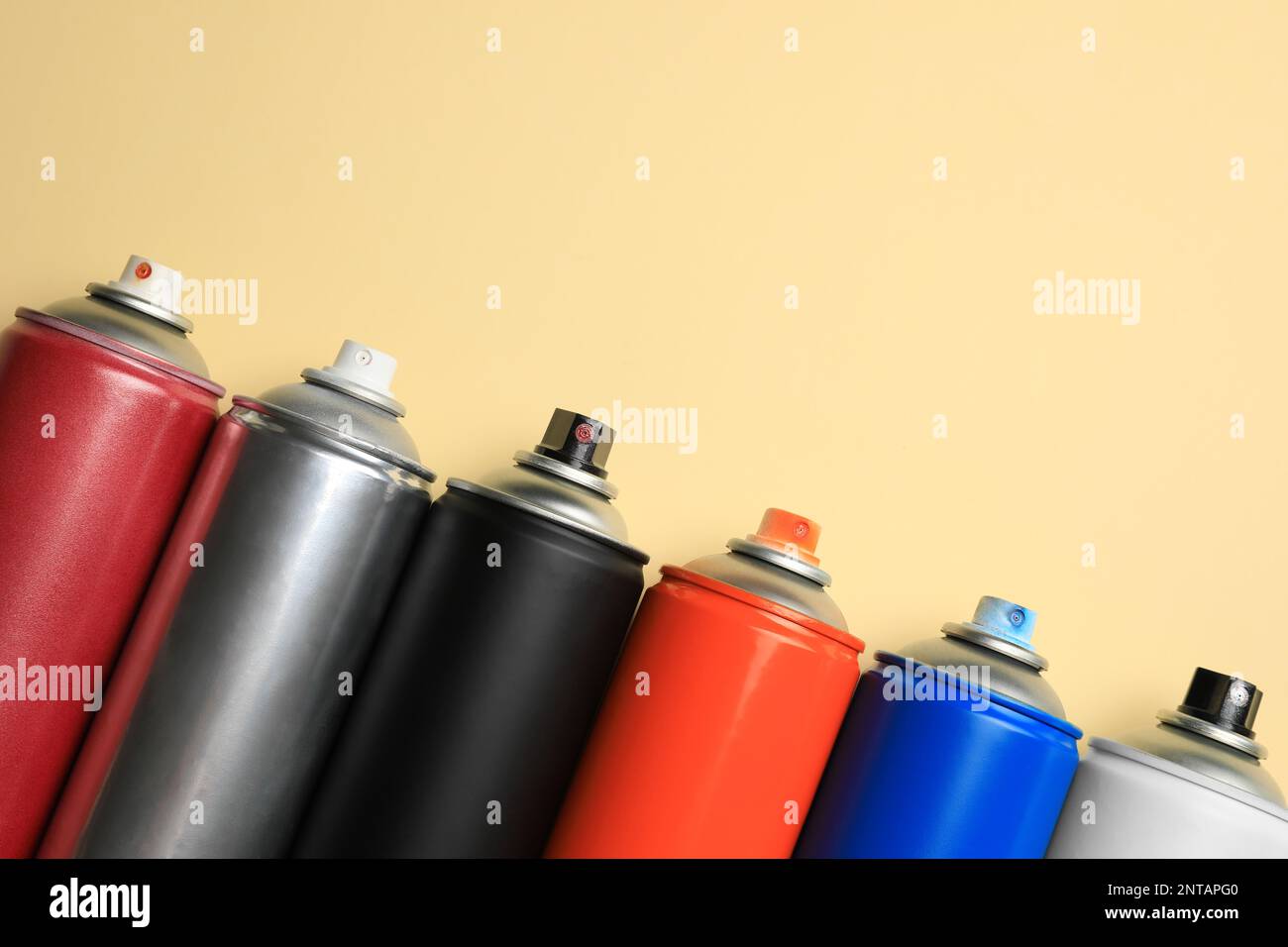 Cans of different spray paints on beige background, flat lay with space ...