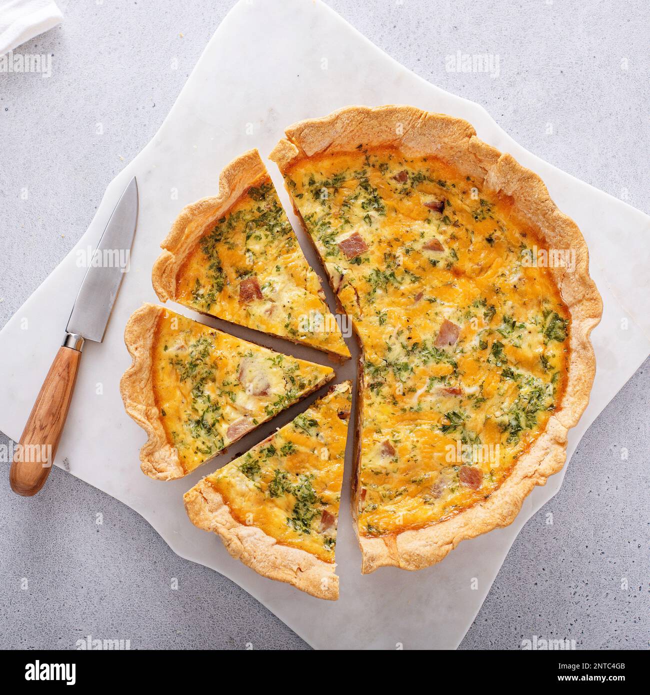 Homemade quiche with ham, cheddar cheese and parsley cut on the table ...