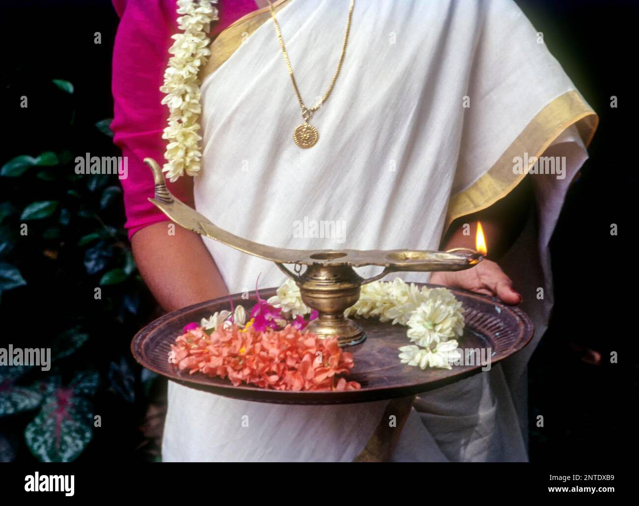 A girl holding oil lamp and flowers on a tray during Onam festival ...