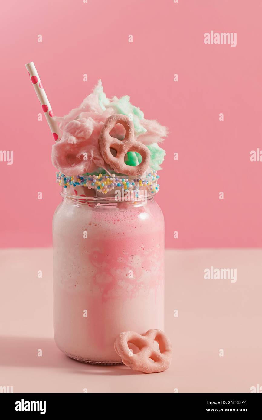 Milkshake in a glass jar covered with a cotton candy, pink background ...