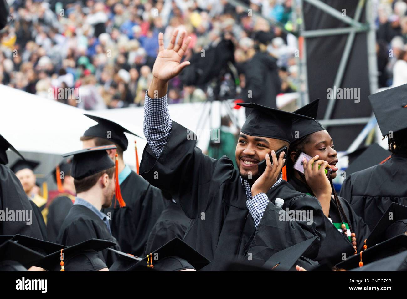 A graduate waves while speaking on a cell phone at the commencement ...