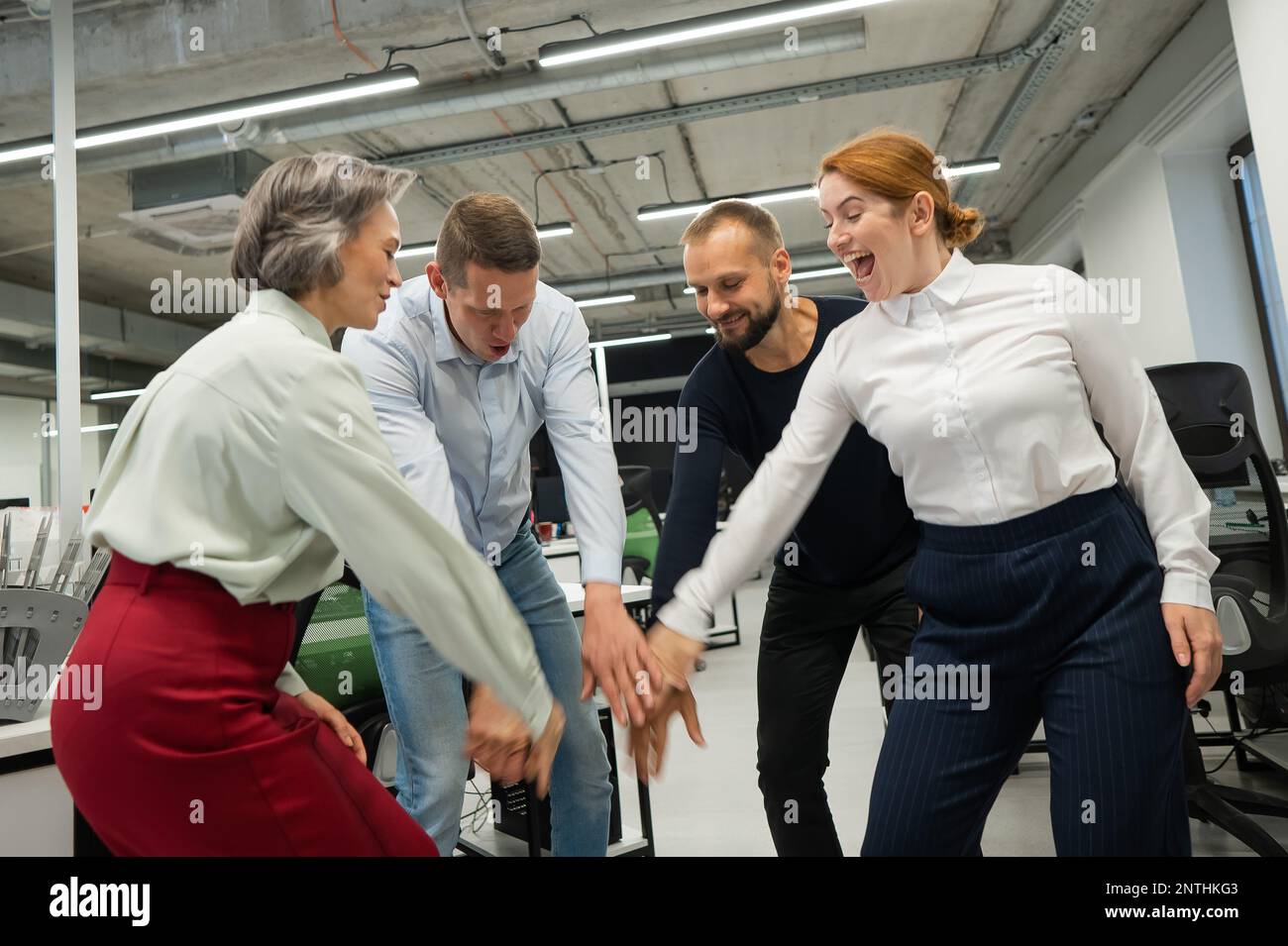 Four colleagues give the low five in the office Stock Photo - Alamy