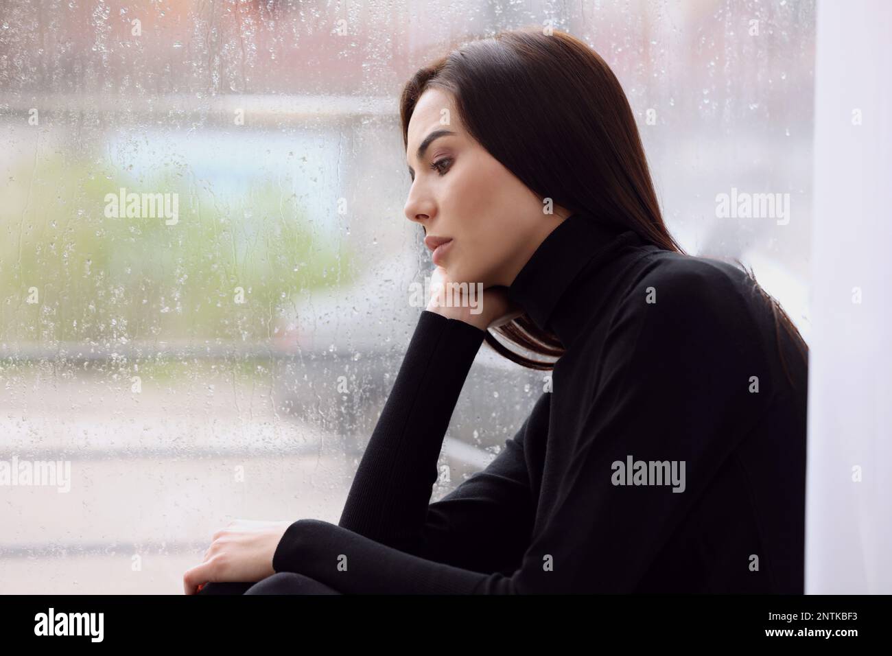 Depressed woman near window on rainy day, space for text Stock Photo ...
