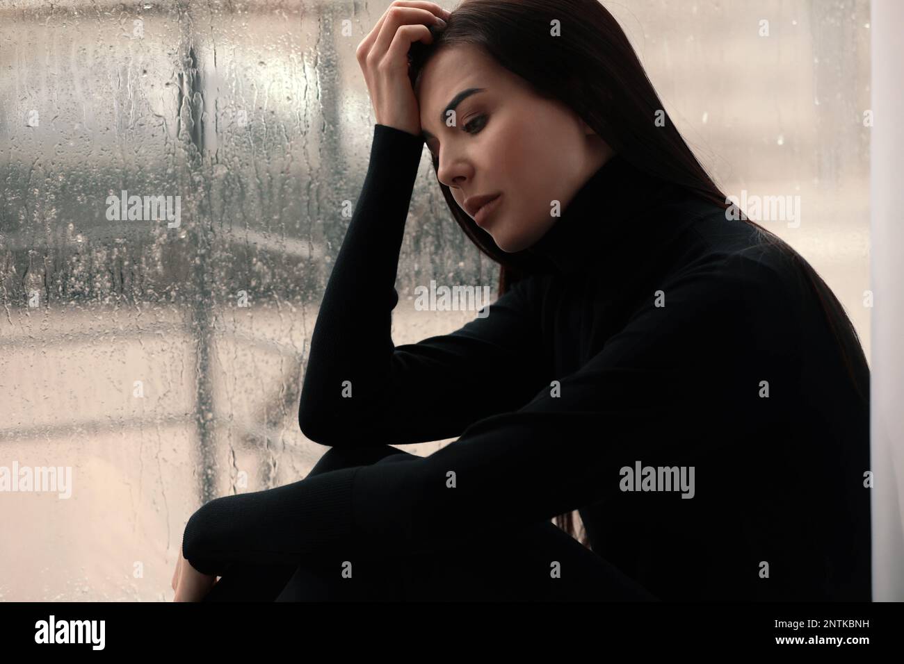 Depressed woman near window on rainy day Stock Photo - Alamy