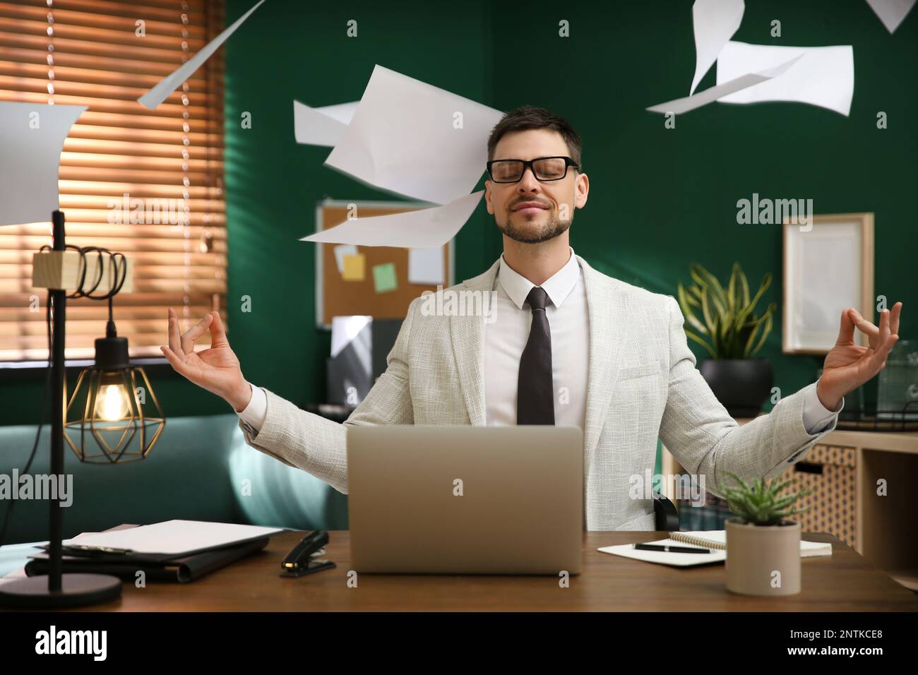 Calm businessman meditating at office desk in middle of busy work day ...