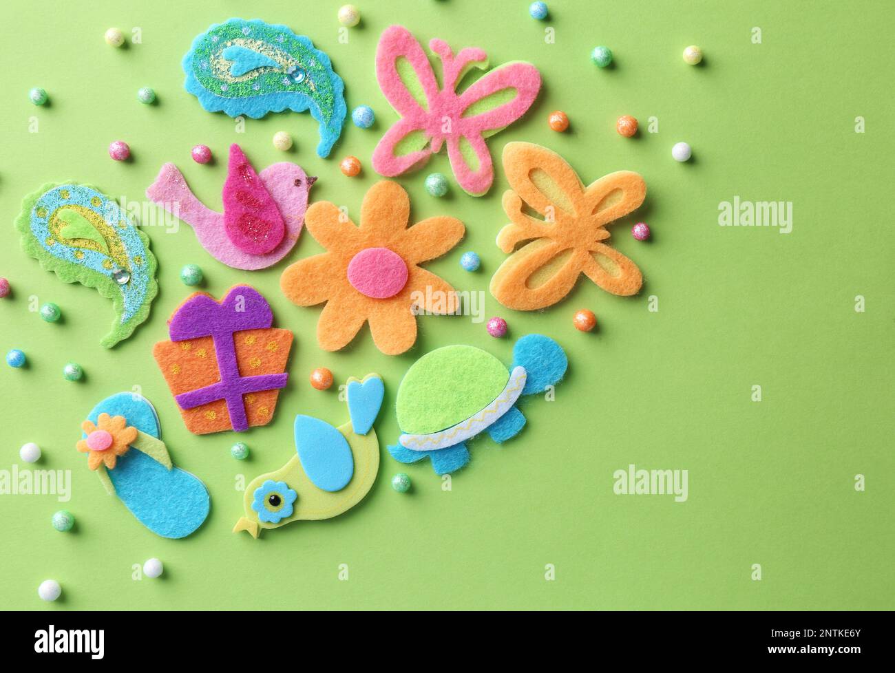 Different small colorful felt items and beads on green background, flat ...