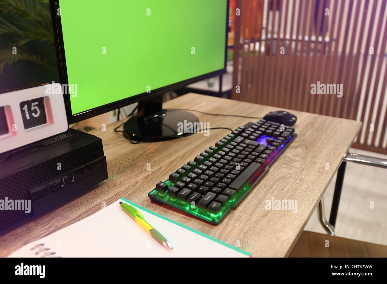 Modern computer and RGB keyboard on wooden table indoors. Mockup green ...