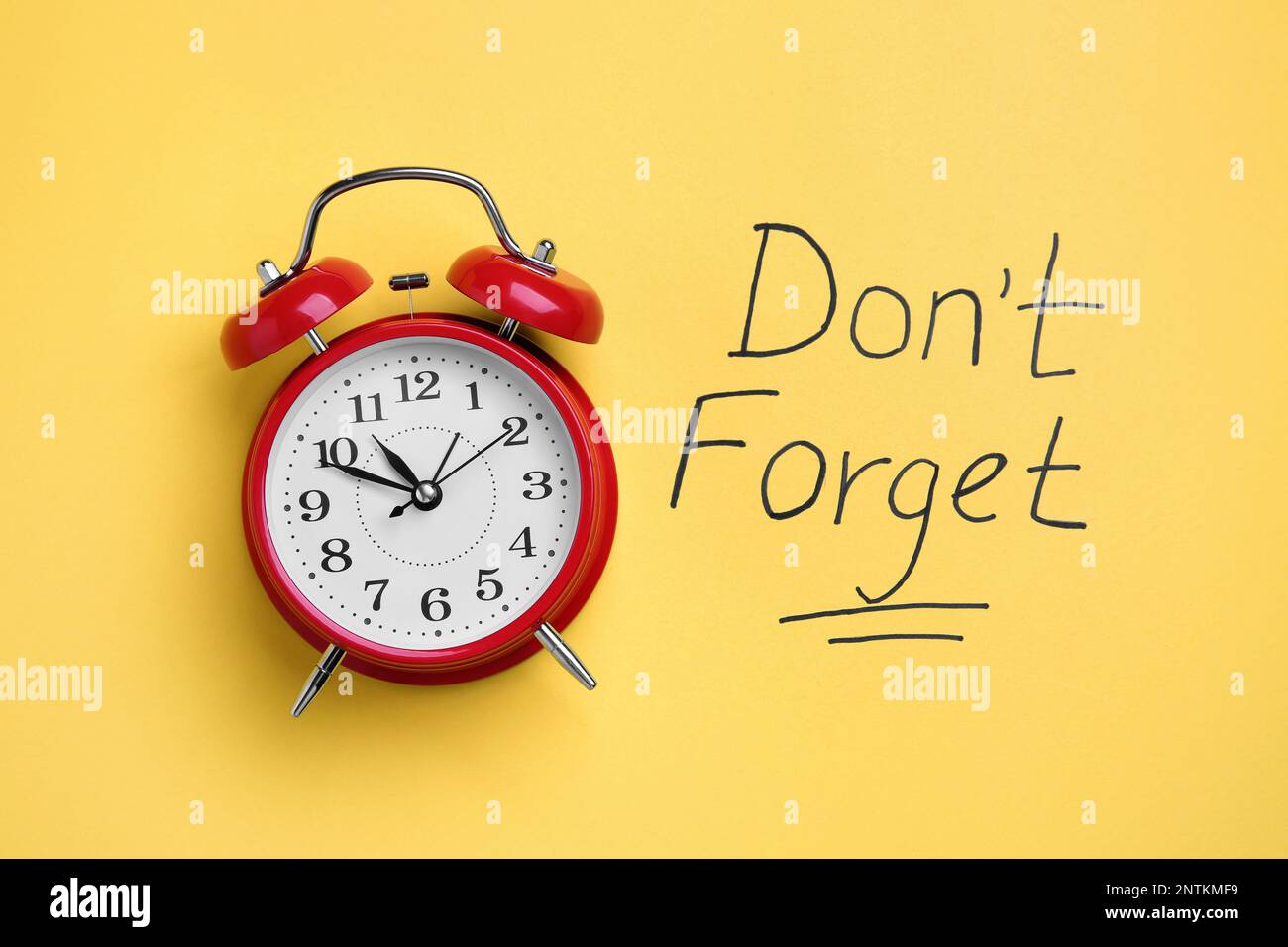 Alarm clock and text Don't forget on yellow background, top view ...