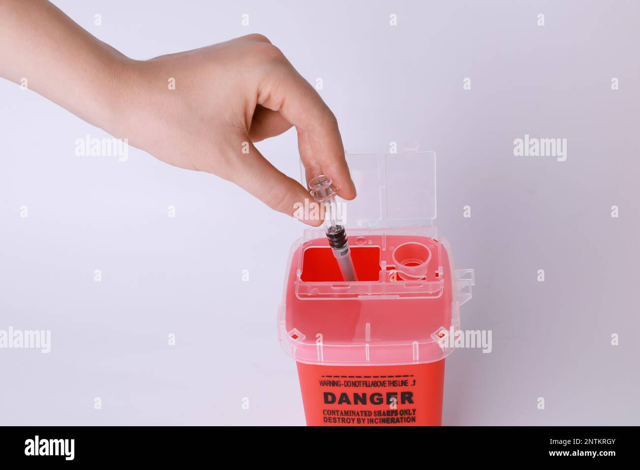 Woman throwing used syringe into sharps container on white background ...