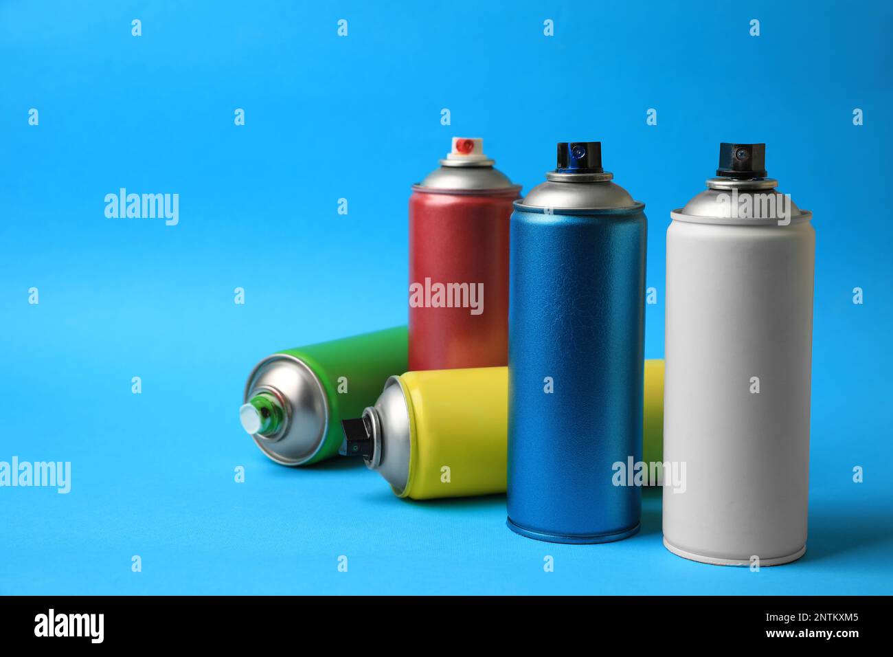 Cans of different graffiti spray paints on light blue background, space ...