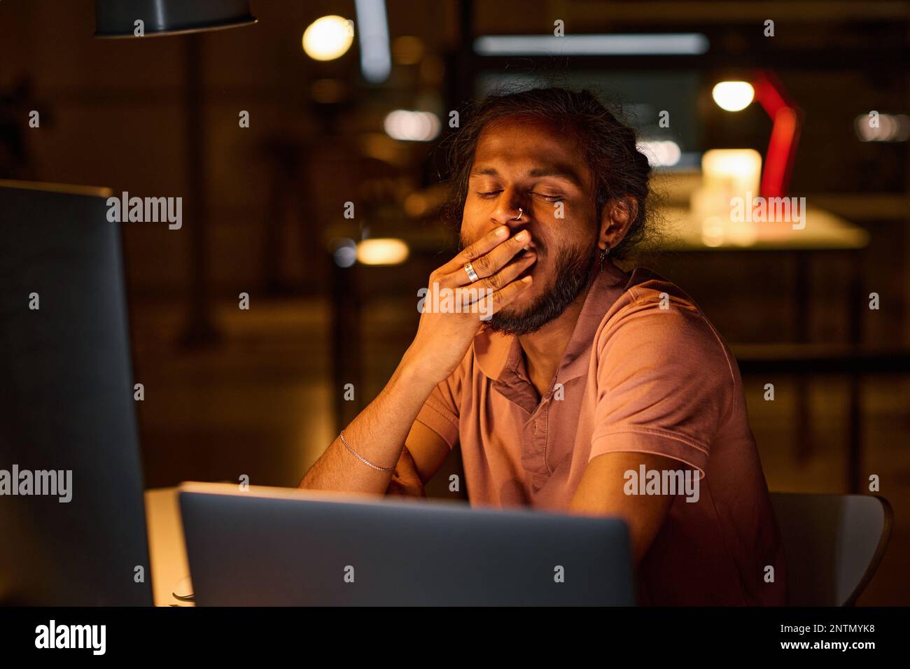 Young developer sitting at his workplace with computer and yawning, he ...