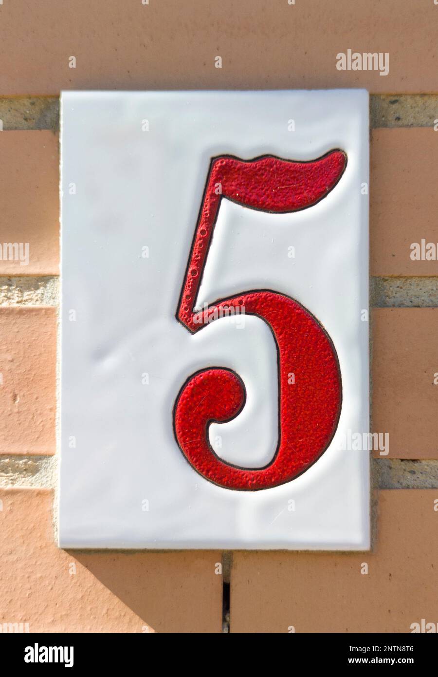 House number 5 over brick sunny wall. Houses with personality concept ...