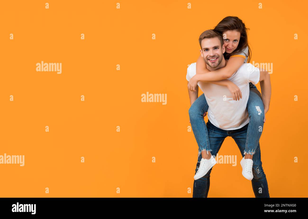 Happy romantic couple having fun doing piggyback ride yellow background ...