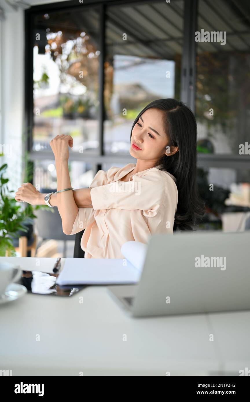 Attractive millennial Asian businesswoman stretching her arms at her ...