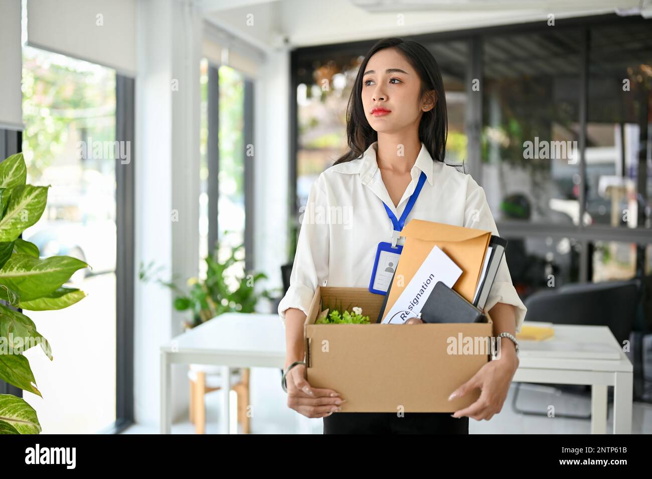 Sad and upset millennial Asian female office worker carrying her belonging, quitting a job ...