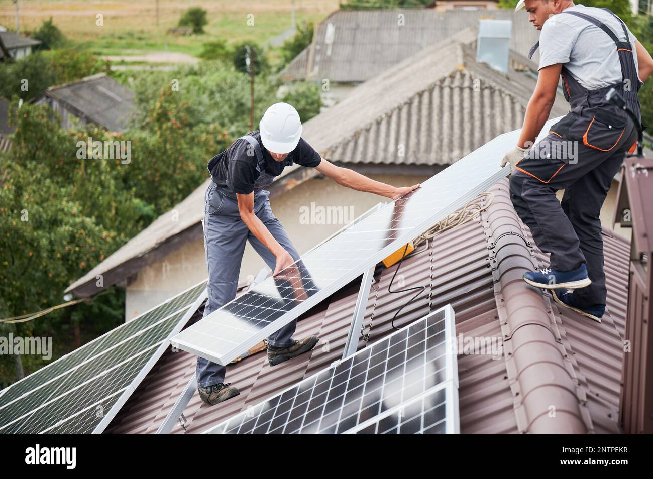 Men technicians carrying photovoltaic solar moduls on roof of house ...