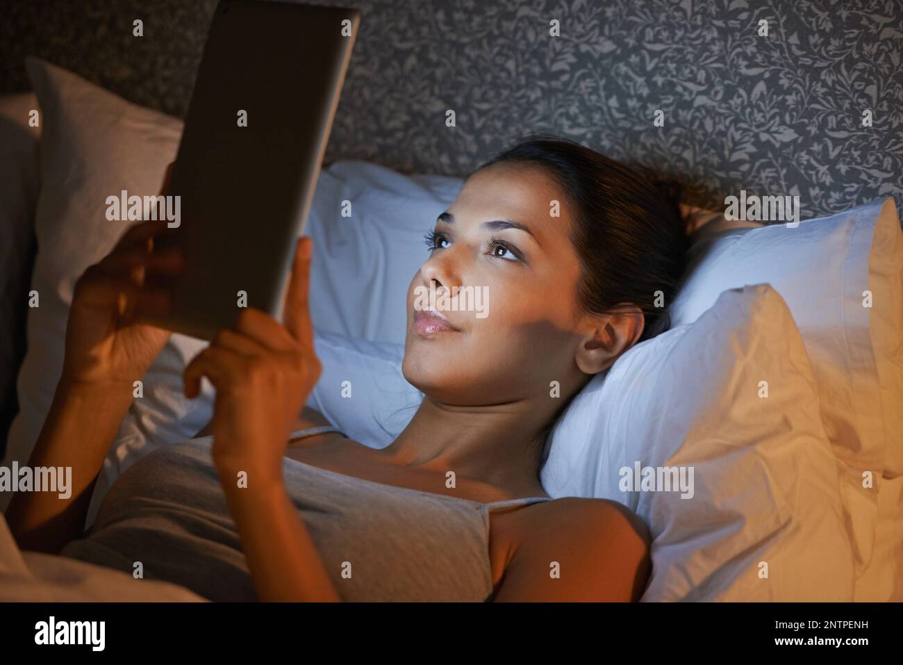 Bedtime bliss. Beautiful young woman playing on her digital tablet before bed Stock Photo - Alamy
