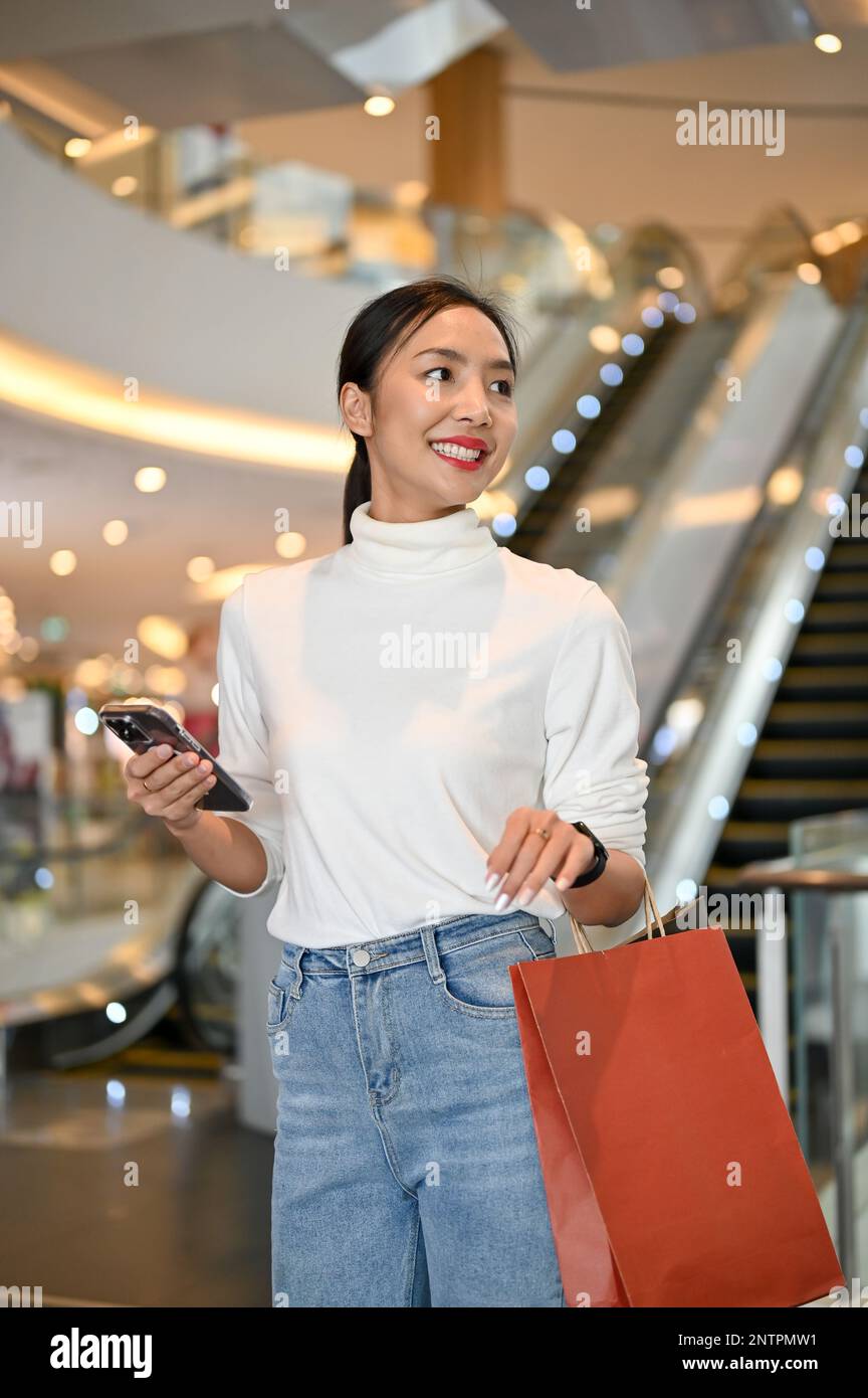 Happy and beautiful millennial Asian woman in trendy clothes carrying ...