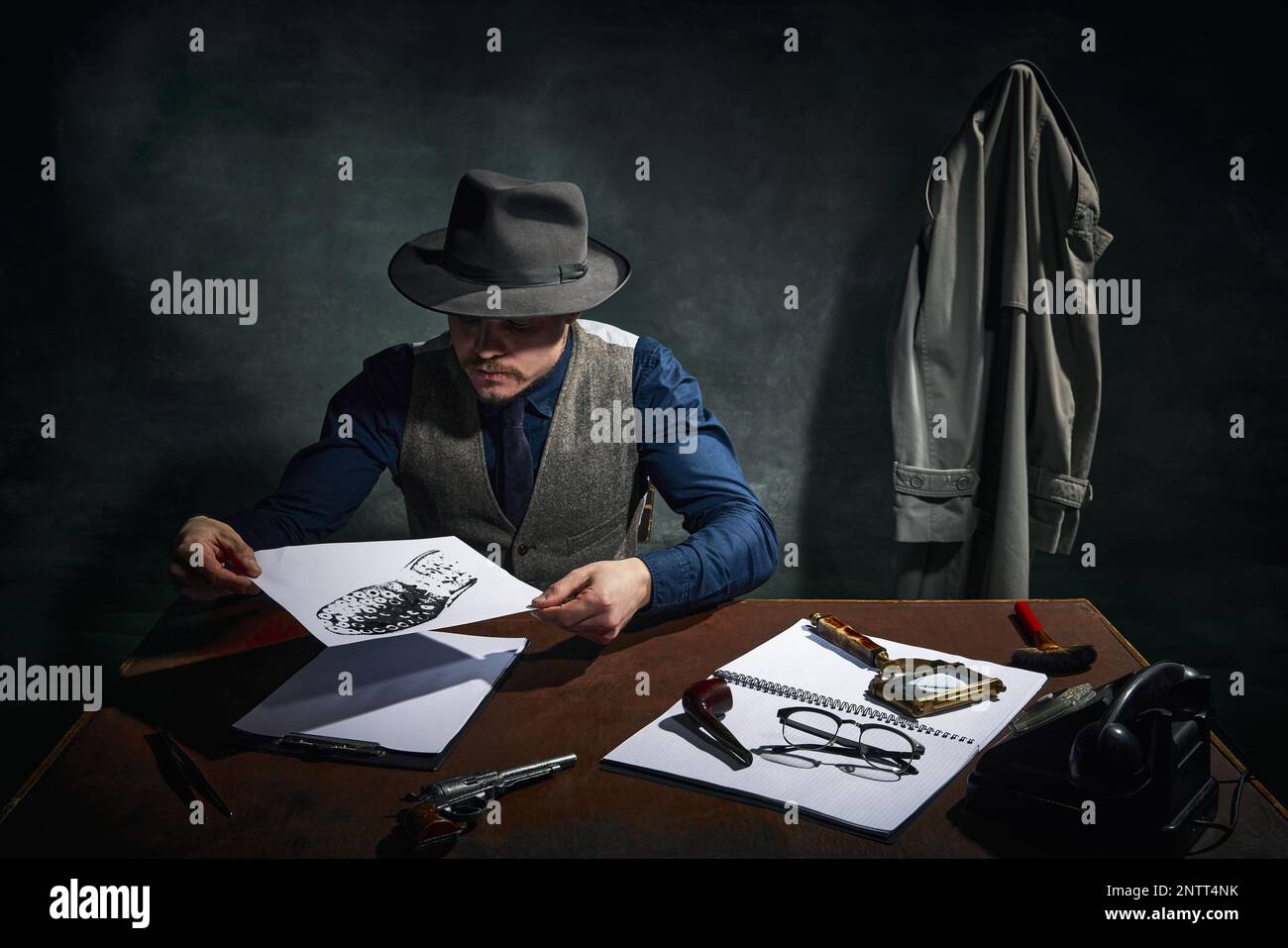 Professional detective in fedora hat sitting at table and looking at ...