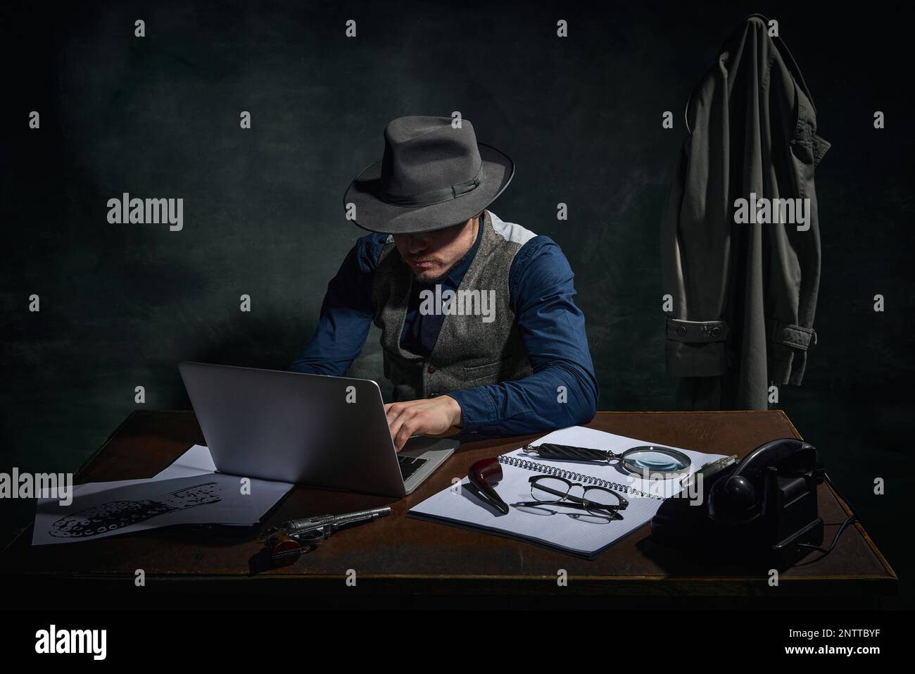 Professional detective in fedora hat sitting at table and working on ...