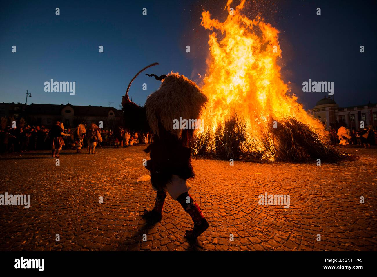 A reveller wearing sheepfur costume and mask dances next to a bonfire ...