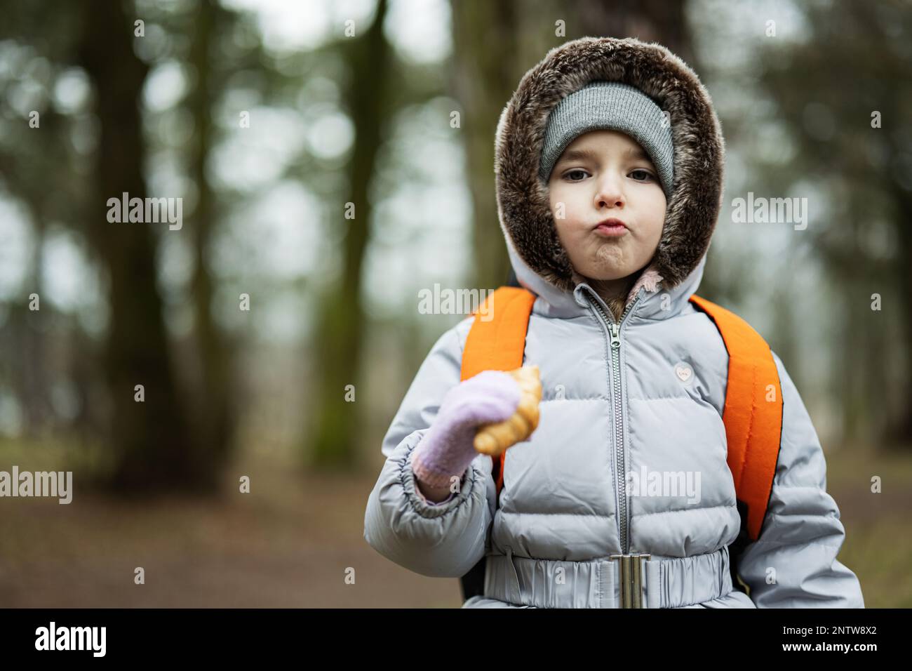 Girl with backpack eating croissant in the forest Stock Photo - Alamy