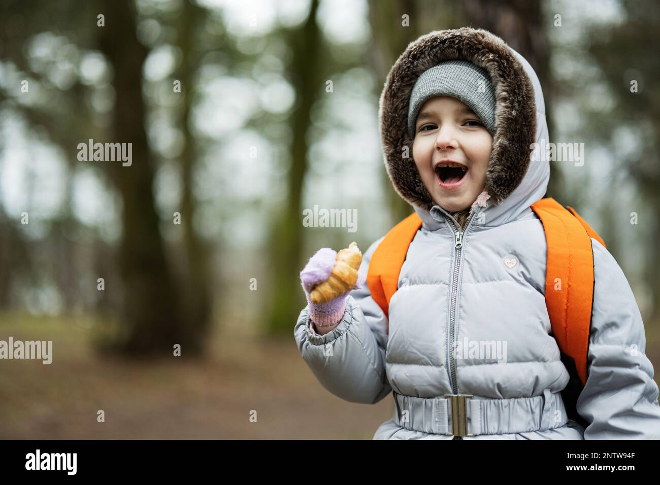 Girl with backpack eating croissant in the forest Stock Photo - Alamy