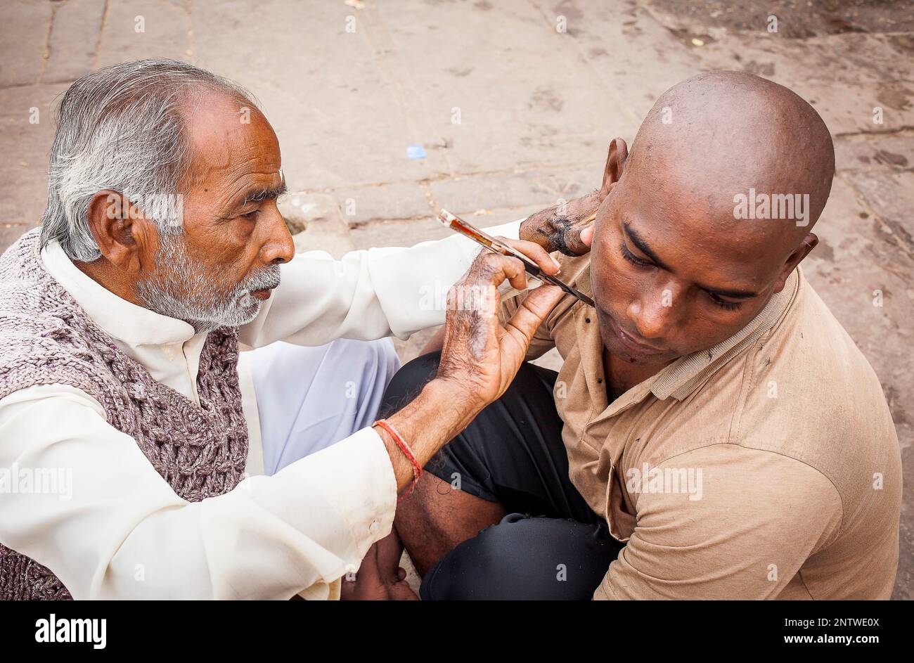 Barber shaving the head and beard of a pilgrim, Dashashwamedh ghat ...