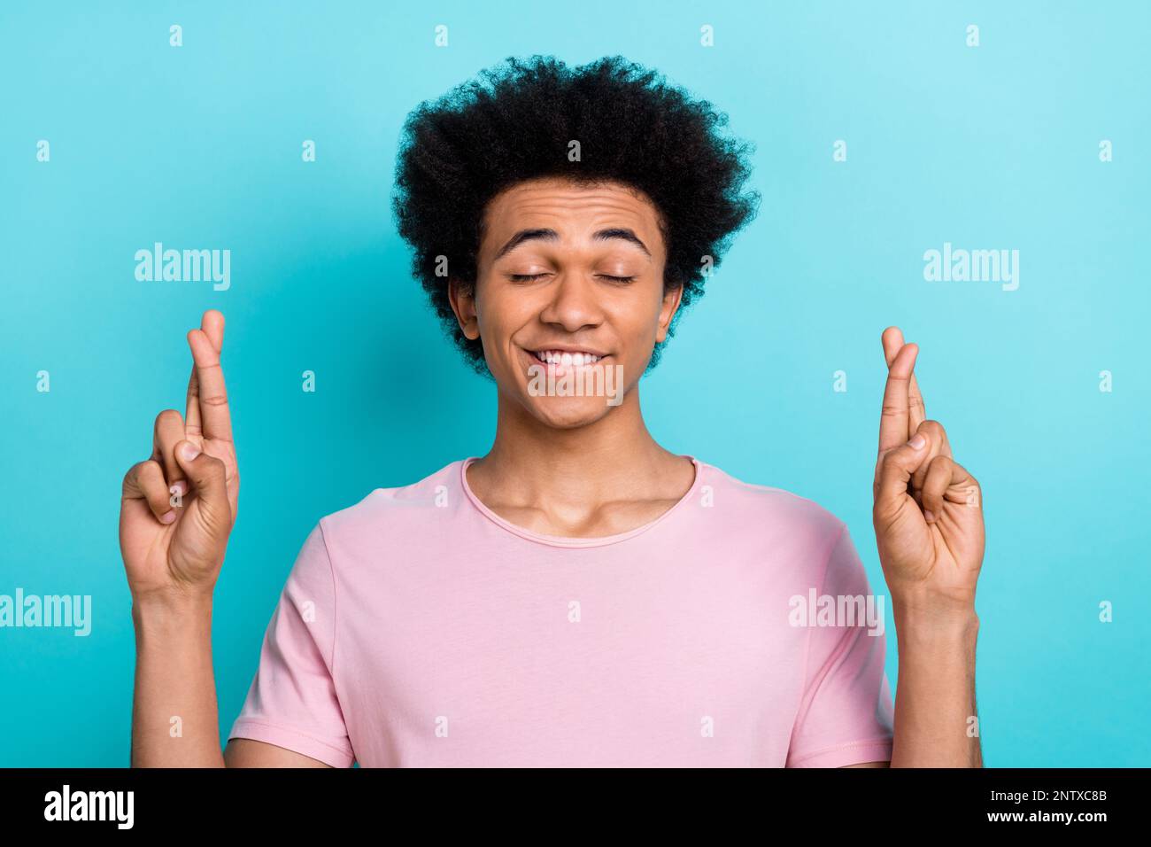 Photo of funny pleading young guy pink t-shirt crossed fingers closed ...