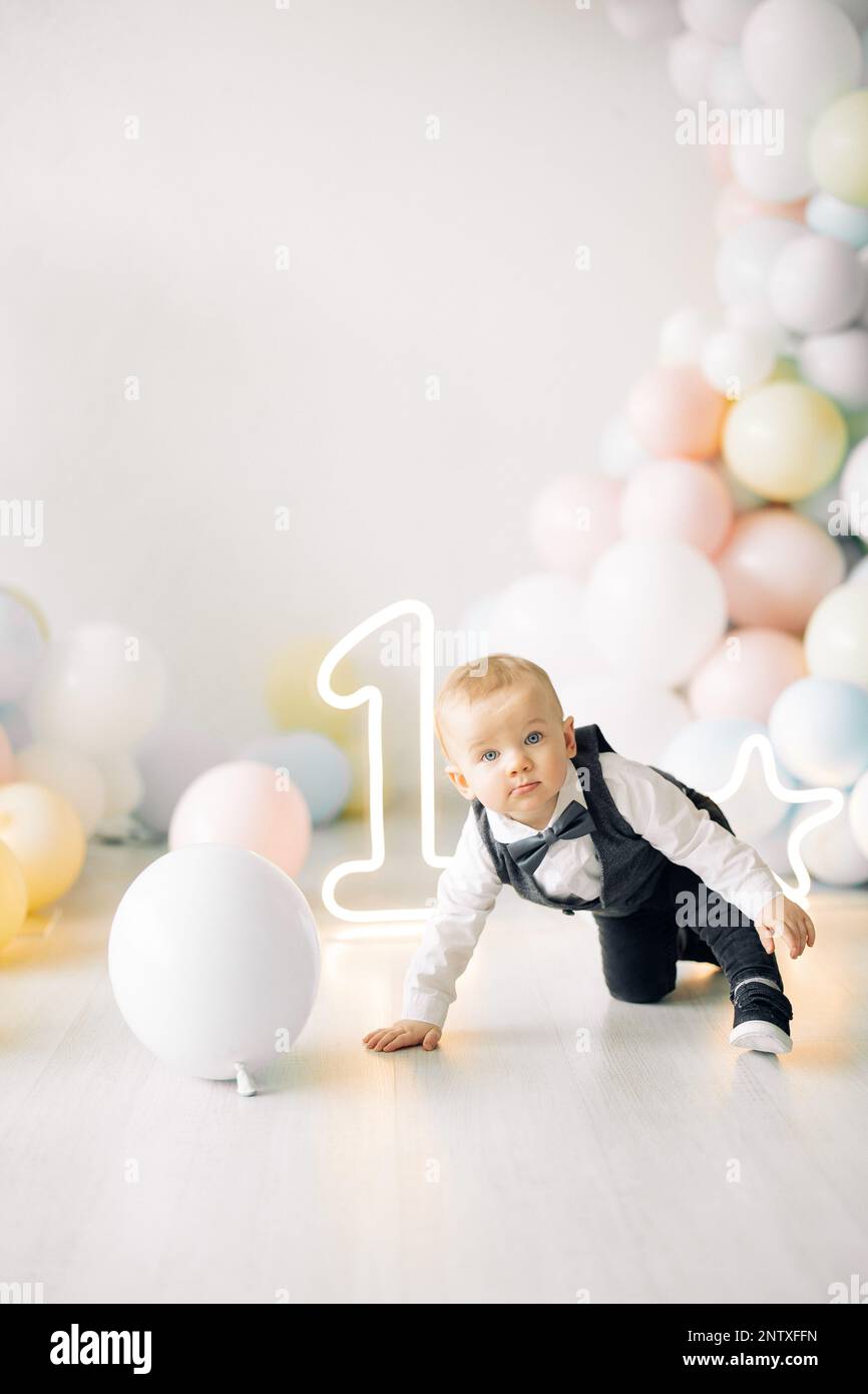 One year old boy is crawling on floor among a lot of colorful balloons ...