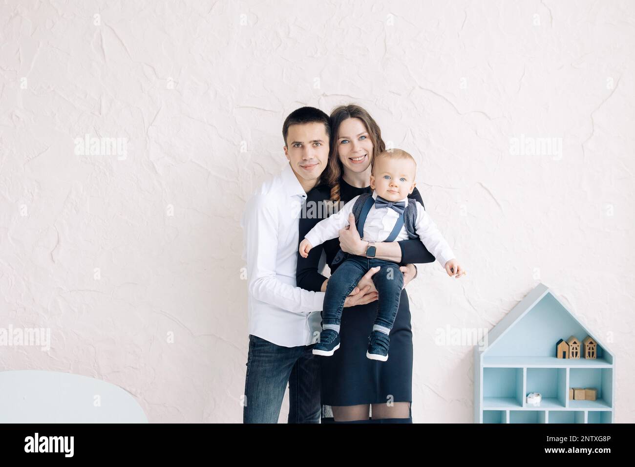 Young happy parents stand and pose with their toddler boy against white ...
