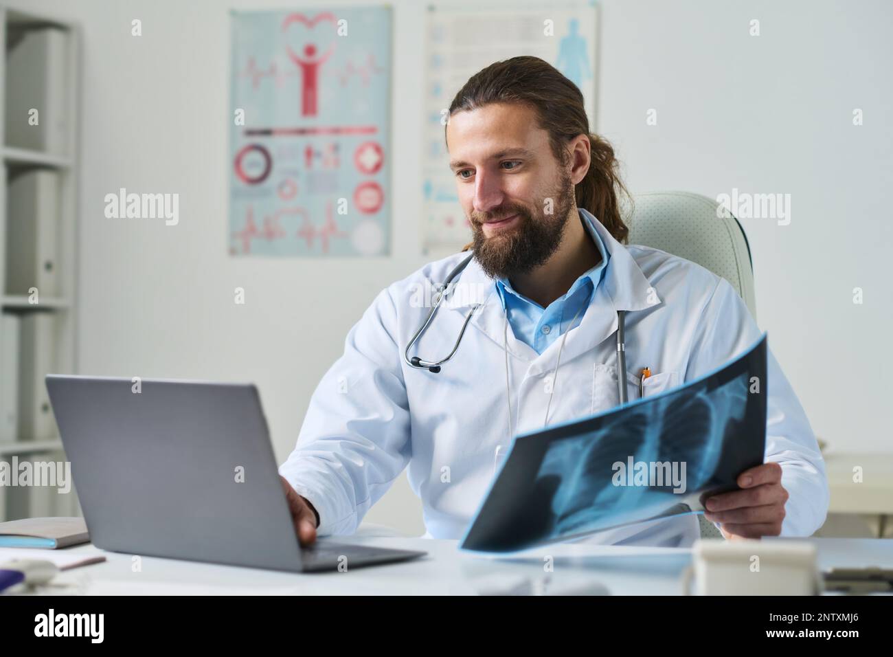 Young smiling general practitioner with x-ray image looking at online ...