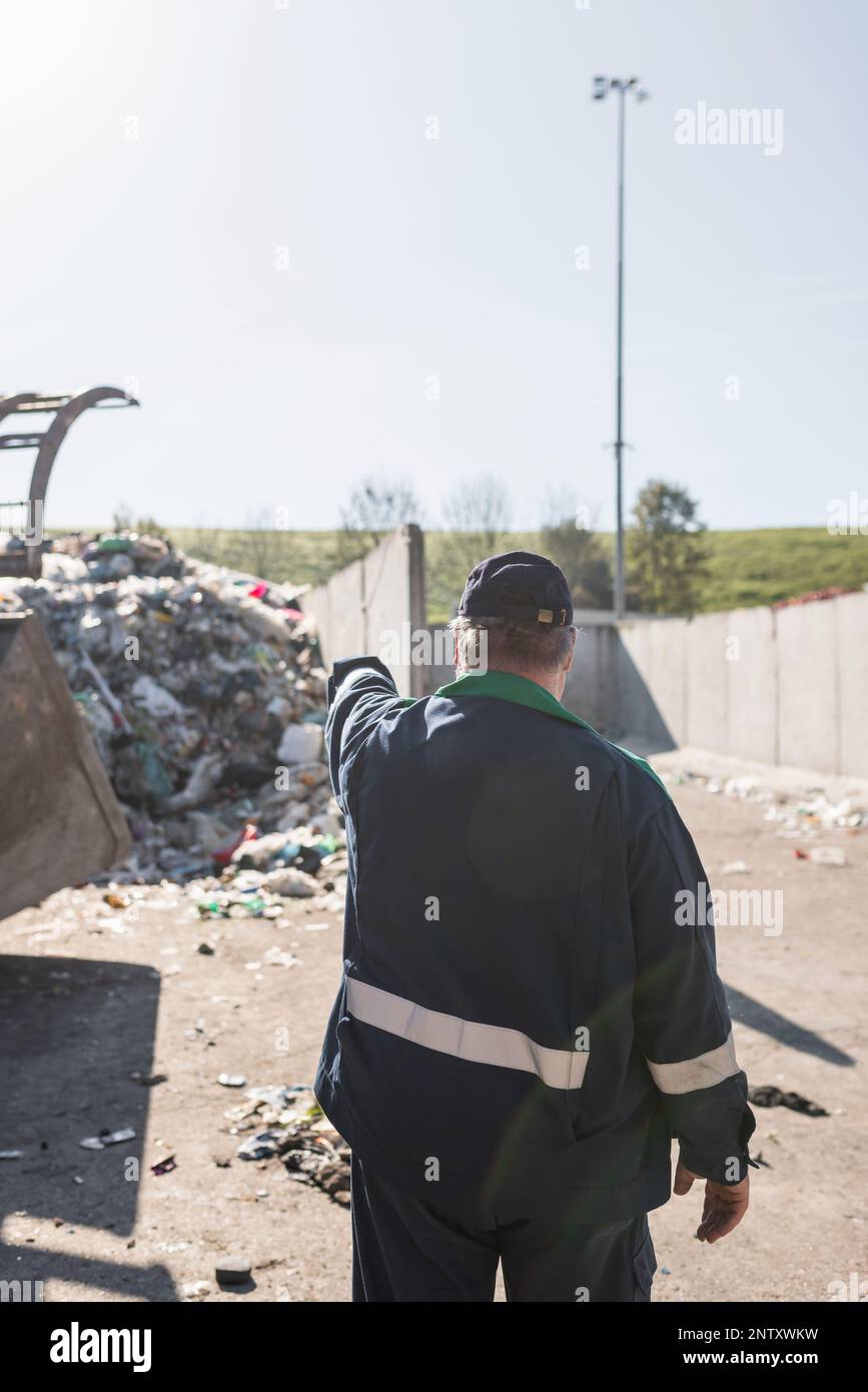 Landfill worker directing skid steer loader on the garbage heap. Waste ...