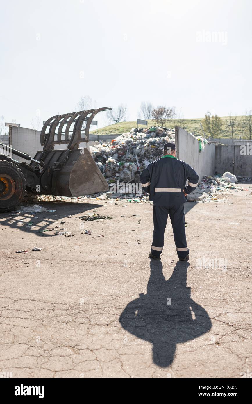 Recycling center worker, in dark blue work clothes, looking at an ...