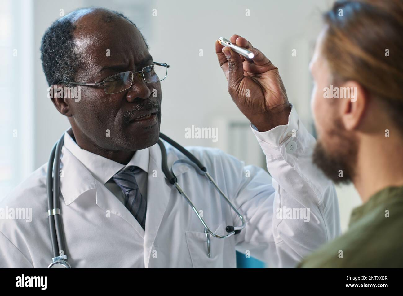 Mature male clinician with special medical device directing light on ...