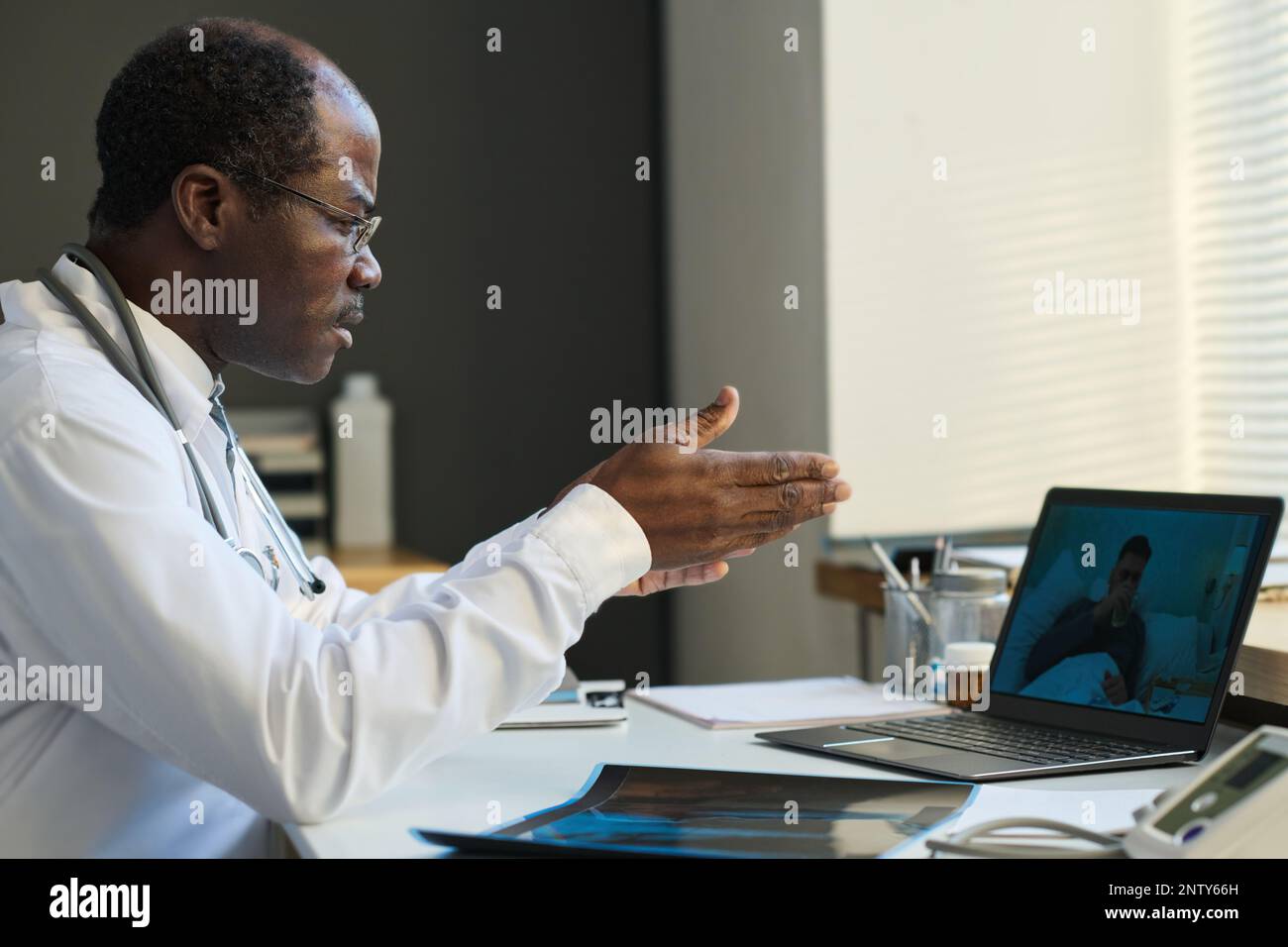 Confident mature teledoc sitting by workplace in front of laptop with ...
