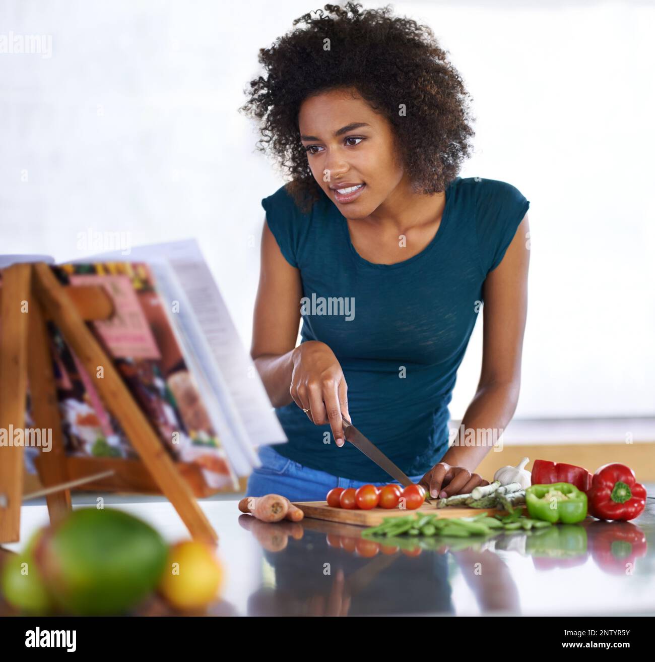Am I doing this correctly. A young woman cooking from a recipe book ...
