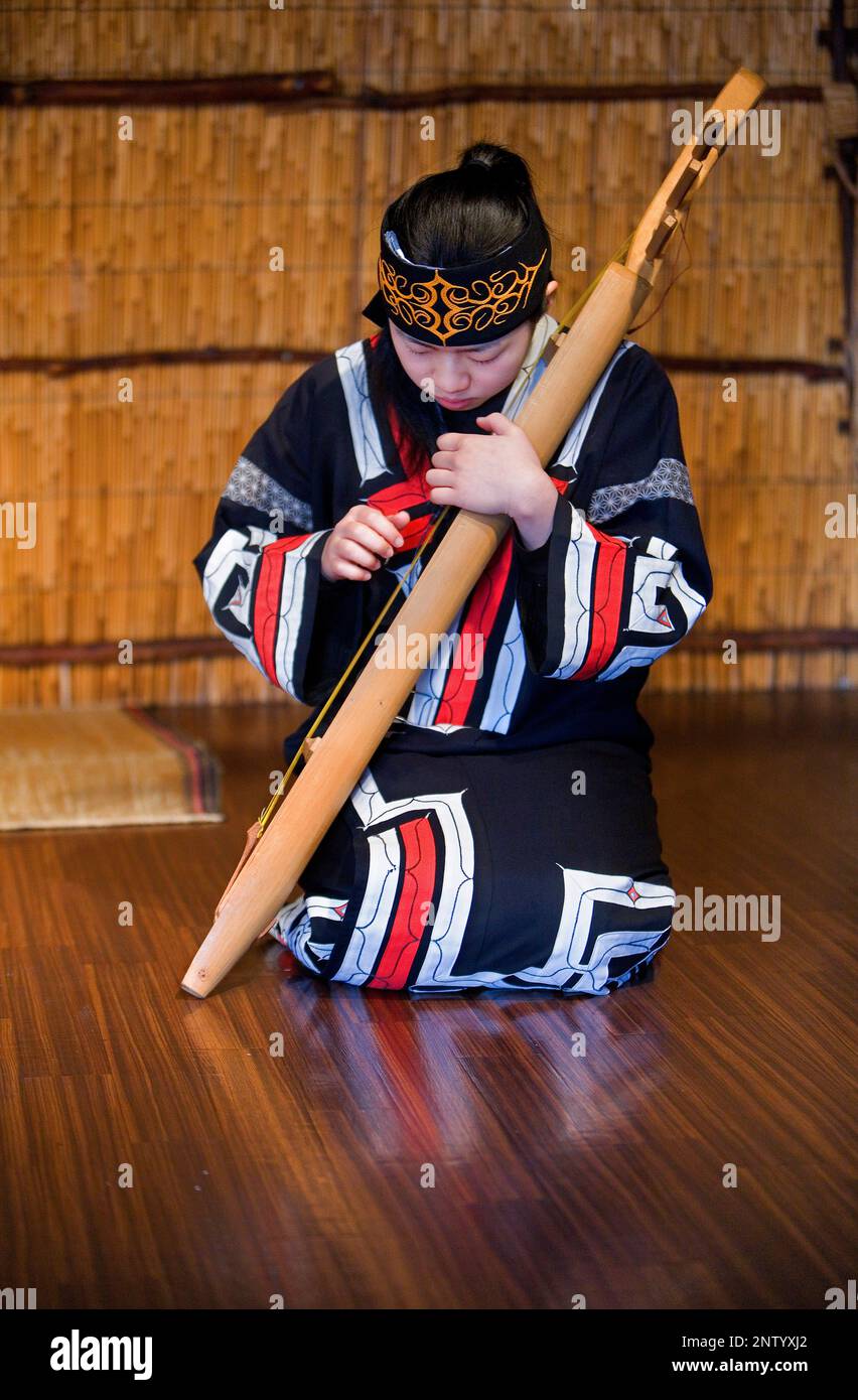 Ainu woman playing a traditional instrument in Ainu village museum ...