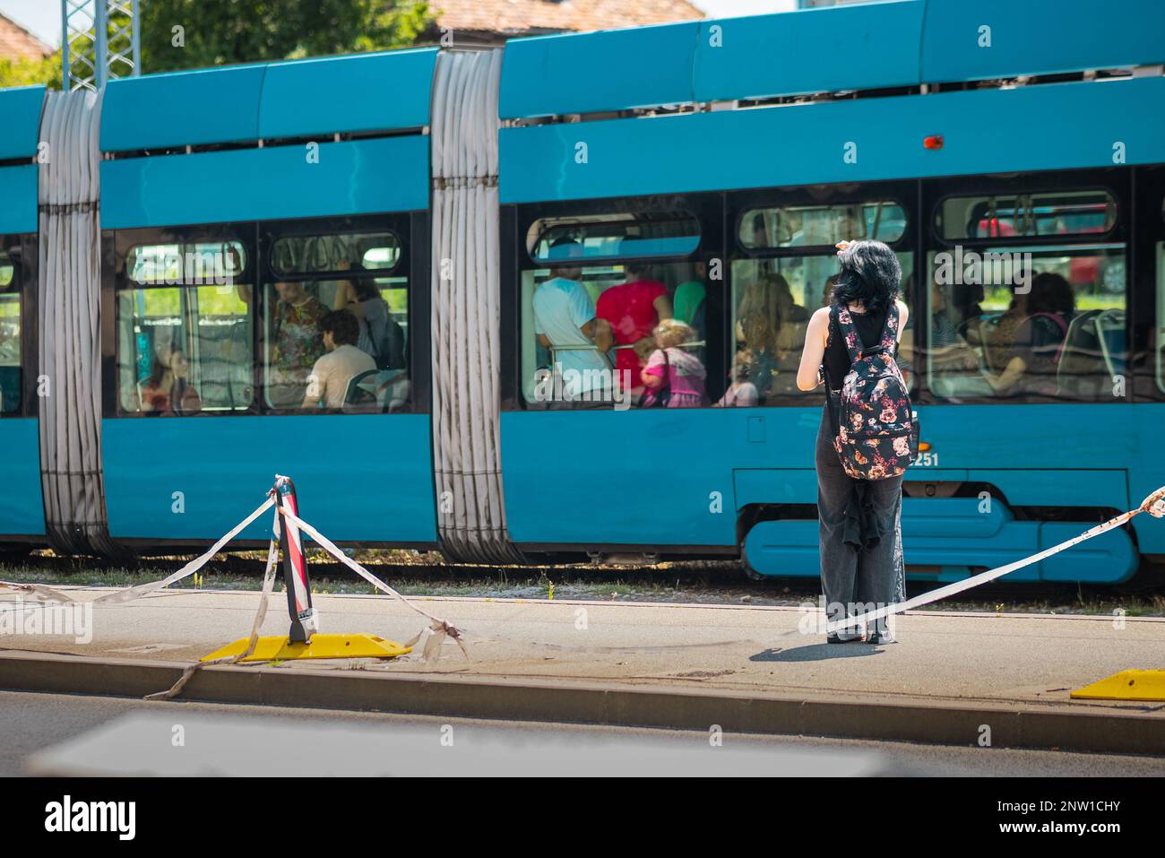 Unknown female viewed from behind is waiting to board a blue tram in ...