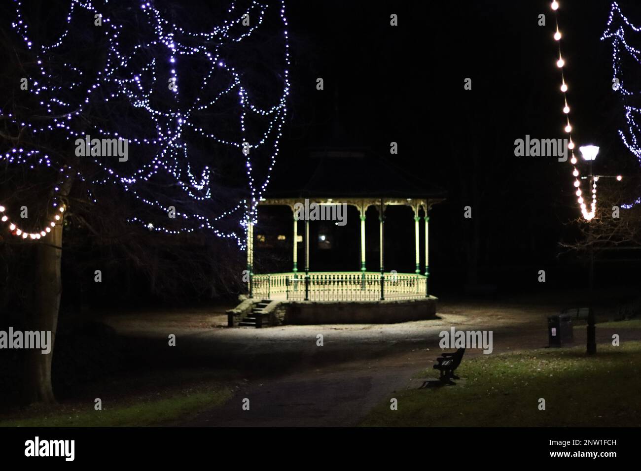 Bandstand in an English town park lit at night and illuminated by tree ...