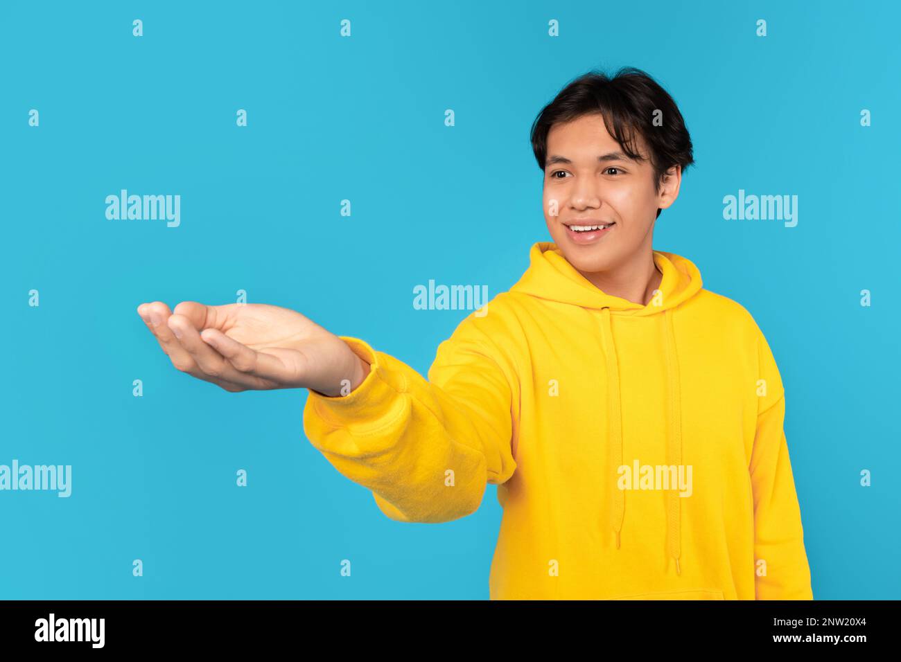Chinese Teen Guy Stretching Hand Showing Something Over Blue Background ...